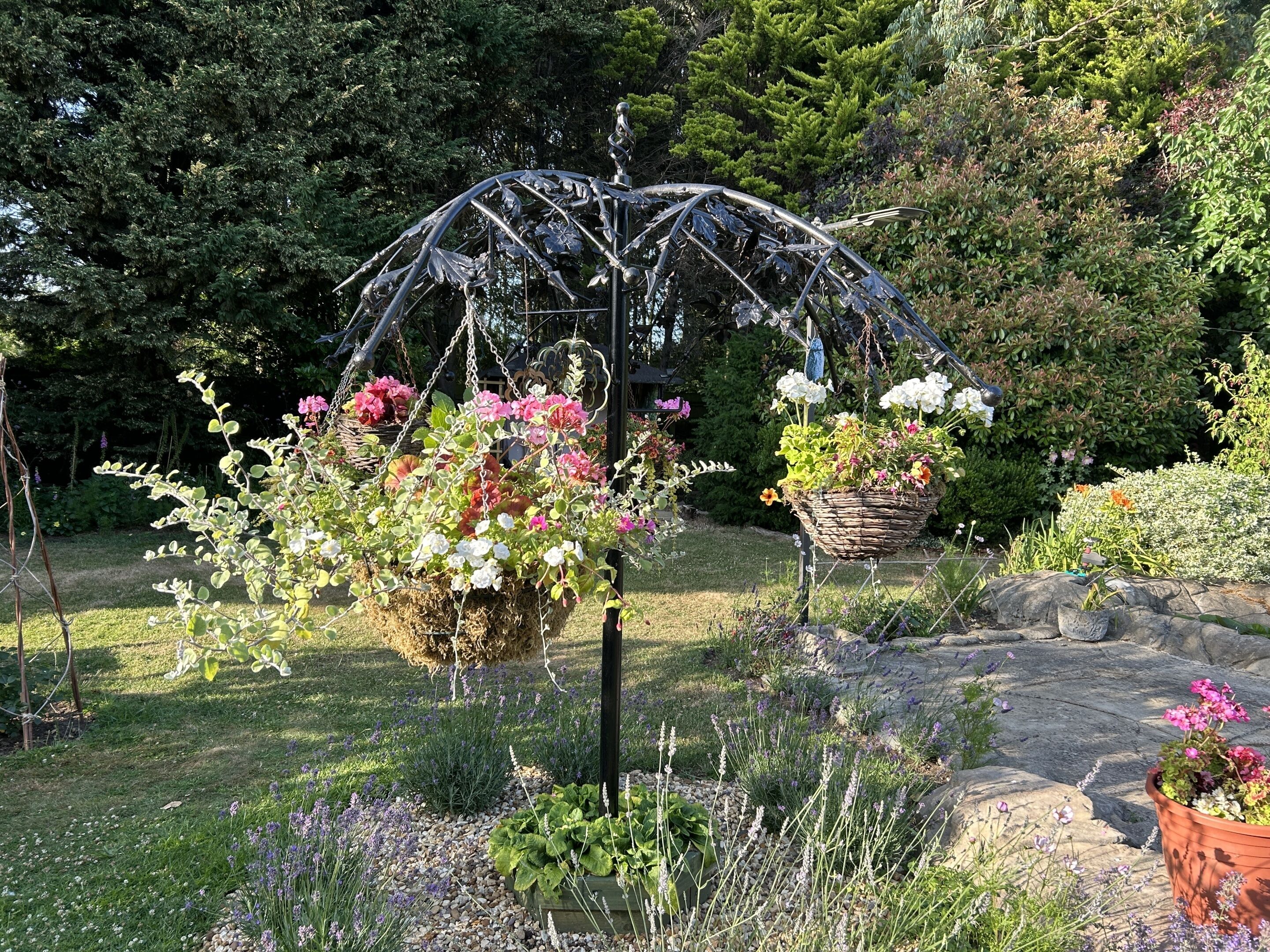 Um jardim com estrutura de treliça de metal, diversos vasos de plantas e um caminho de pedra.