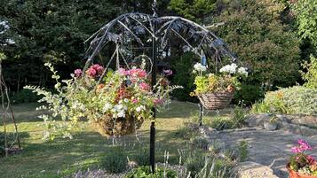Um jardim com estrutura de treliça de metal, diversos vasos de plantas e um caminho de pedra.