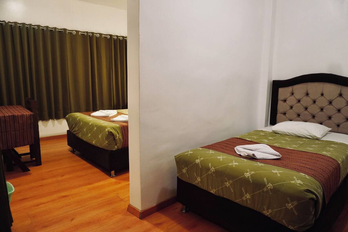 Um quarto com duas camas de solteiro, uma cadeira de madeira e uma mesa pequena.