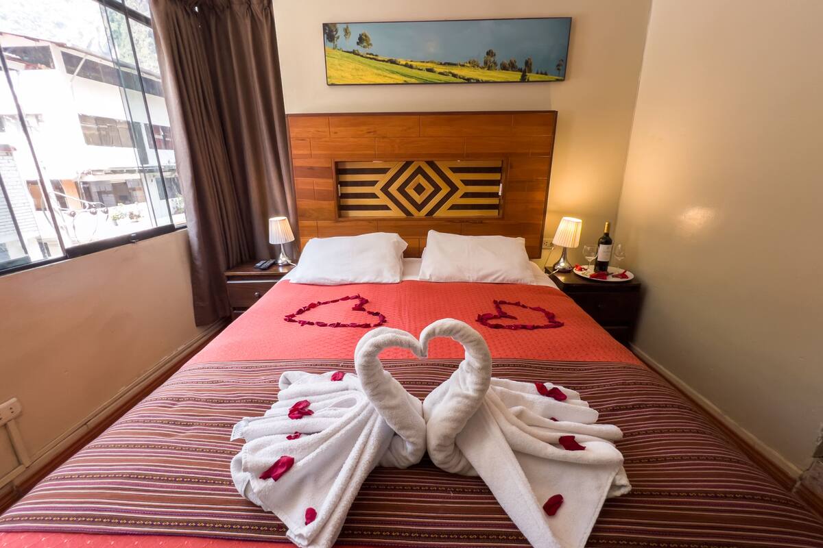 Quarto de hotel com uma cama grande, cabeceira de madeira, um quadro na parede e uma janela com cortinas.