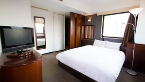 Quarto de hotel com uma cama, televisão sobre um suporte de madeira, espelho, janela com cortinas e abajur.