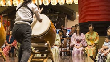 Um ambiente tradicional japonês com um percussionista e público trajando vestes típicas.