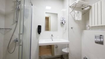 Uma casa de banho moderna com cabine de duche em vidro, lavatório branco, sanita e barra de toalhas.