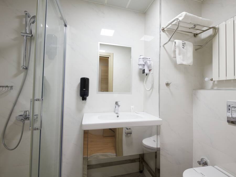 Uma casa de banho moderna com cabine de duche em vidro, lavatório branco, sanita e barra de toalhas.