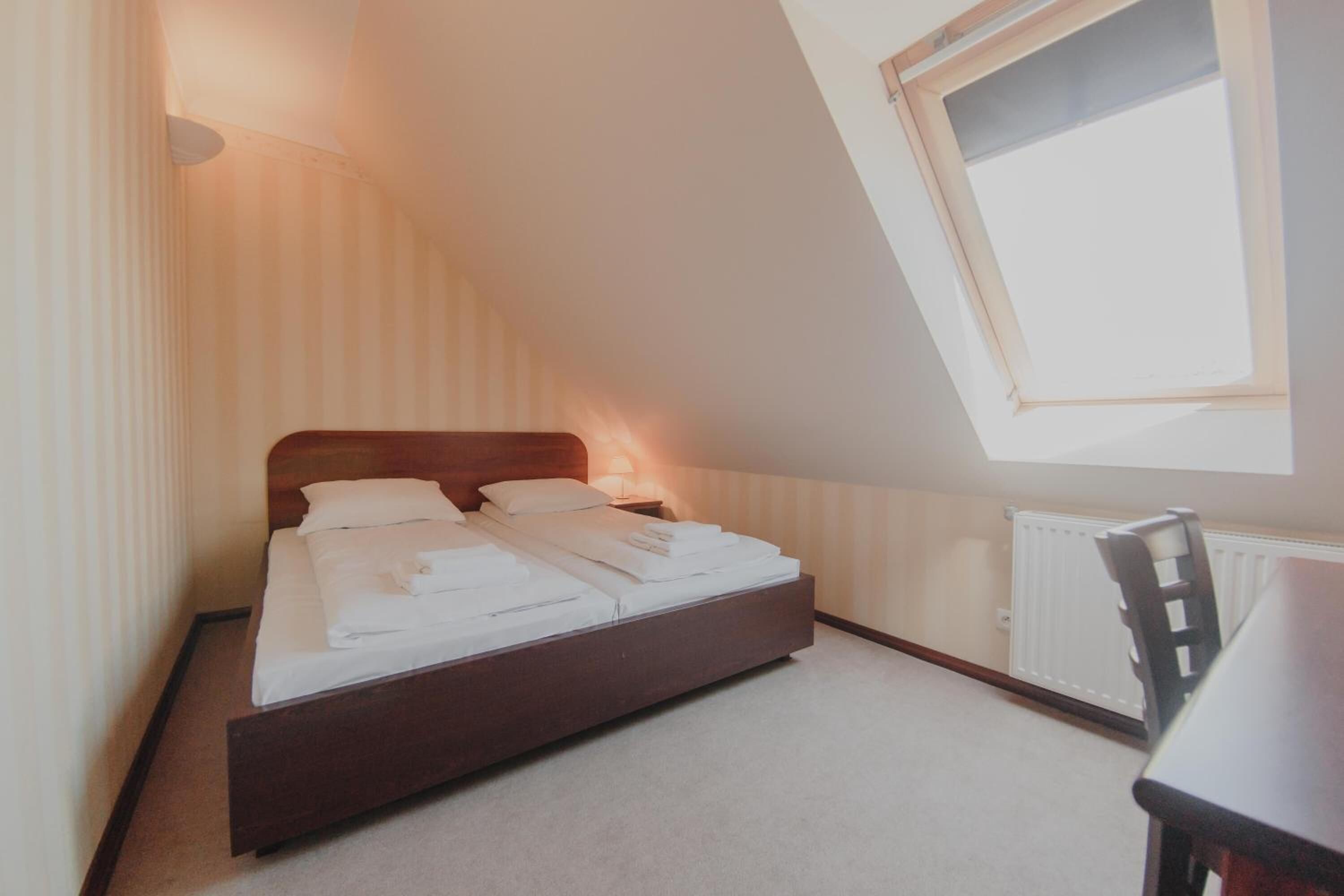 Quarto com cama de madeira, mesa de cabeceira com luminária, radiador e janela com vista.