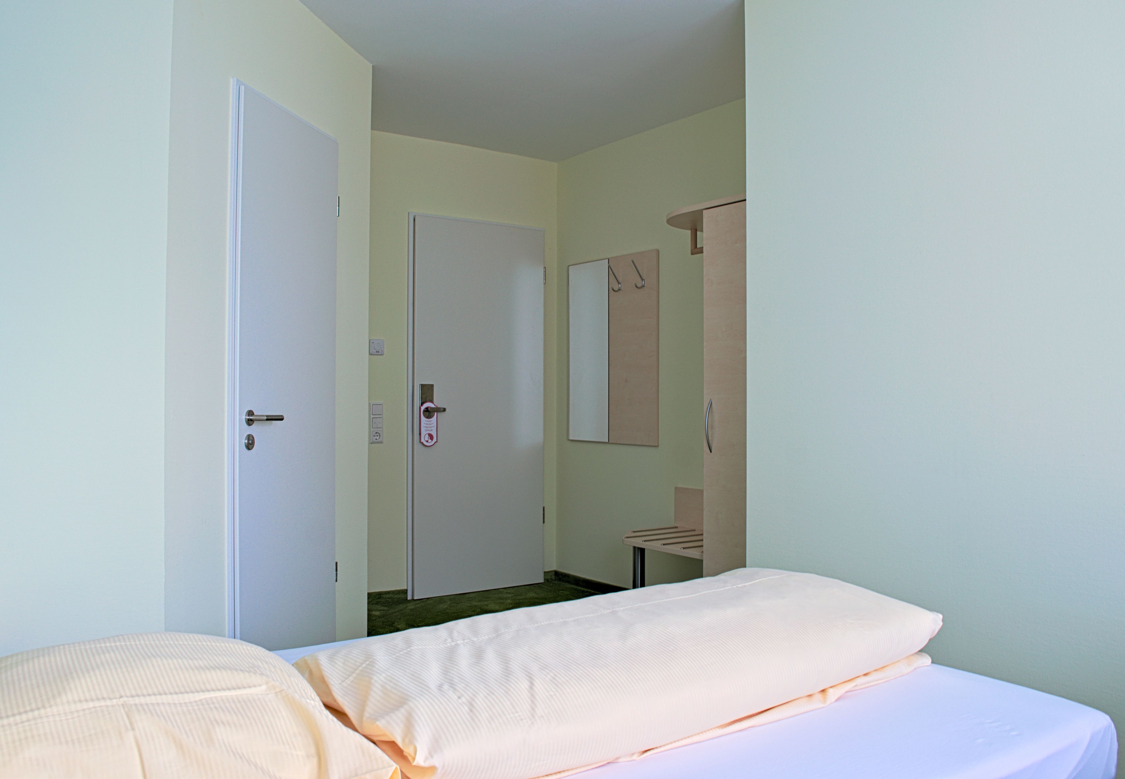 Quarto de hotel com cama, porta, espelho e uma pequena mesa.