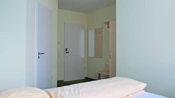 Quarto de hotel com cama, porta, espelho e uma pequena mesa.