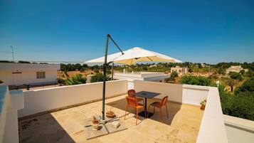 Um terraço no telhado com mesa, cadeiras, um grande guarda-sol e plantas em vasos.
