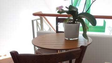 Uma cadeira e uma mesa de madeira sobre um chão de azulejos, com uma orquídea em vaso sobre a mesa.