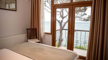 Quarto com cama grande, vista para o mar por uma porta de vidro e uma cadeira de madeira.