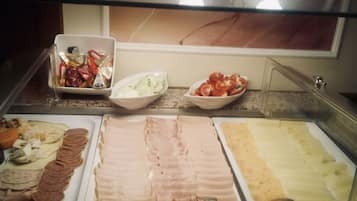 Buffet com diversos itens de comida, incluindo carnes, queijos e frutas.