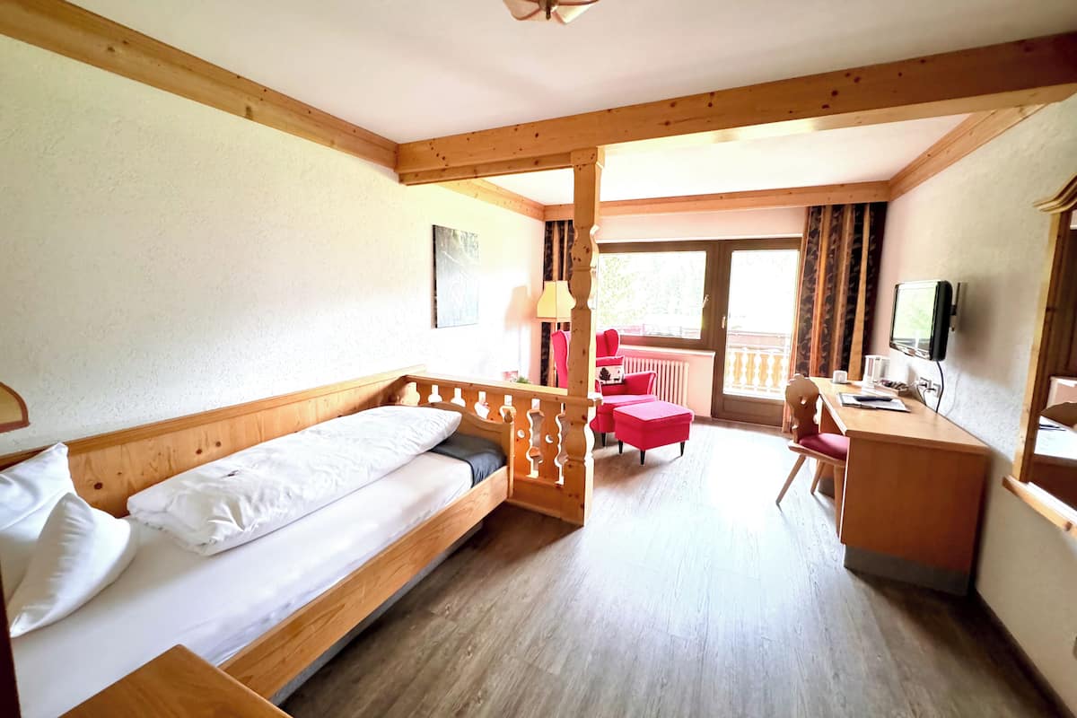 Quarto com cama de madeira, escrivaninha com cadeira, televisão e varanda com vista.