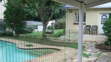 Quintal cercado com piscina, área de varanda coberta e uma casa ao fundo.