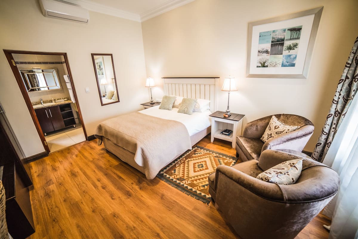 Quarto com cama, duas mesas de cabeceira com abajures, uma cadeira, um tapete, um espelho, um quadro emoldurado e um guarda-roupa.