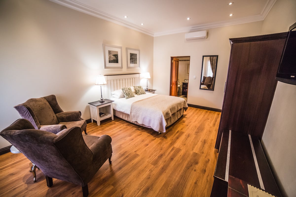 Quarto de hotel com uma cama, duas poltronas, uma mesa de cabeceira e um guarda-roupa.