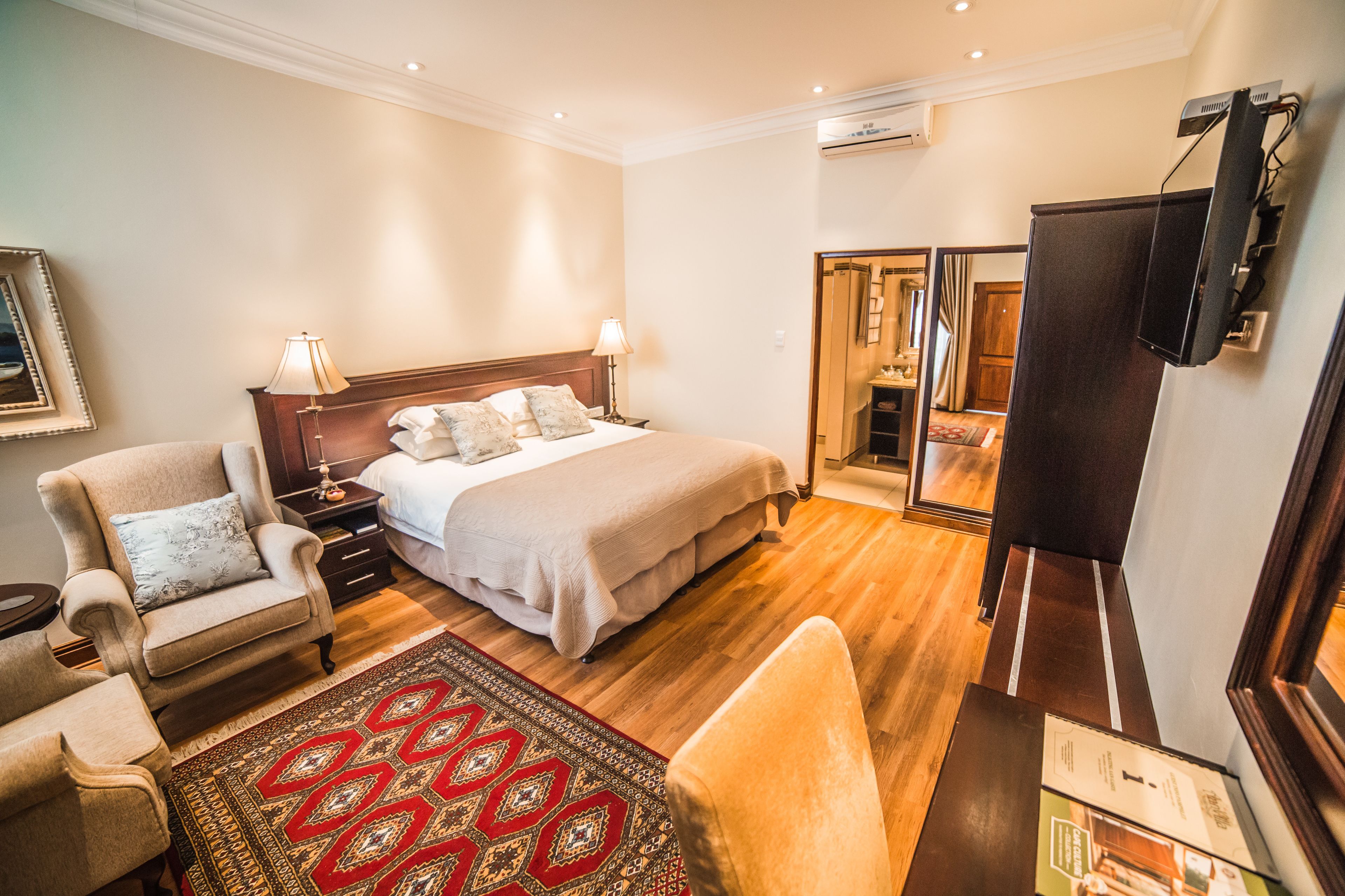 Quarto de hotel com cama, uma cadeira, televisão e piso de madeira.