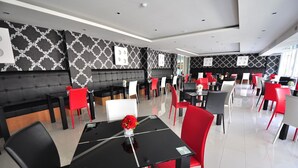 Um restaurante moderno com paredes estampadas em preto e branco, cadeiras vermelhas e brancas, e mesas pretas.
