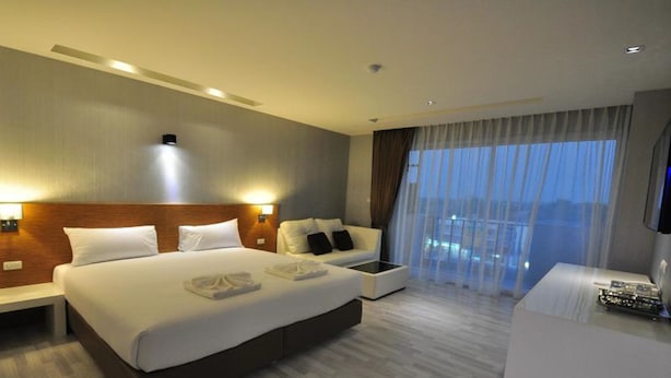 Quarto de hotel moderno com uma cama grande, mesas de cabeceira, escrivaninha e vista da cidade através de amplas janelas.