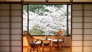Um quarto japonês tradicional com tatames, um painel shoji e vista para as cerejeiras através de uma grande janela.