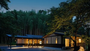 Um edifício tradicional em estilo japonês, com entrada coberta e uma grande árvore na frente.