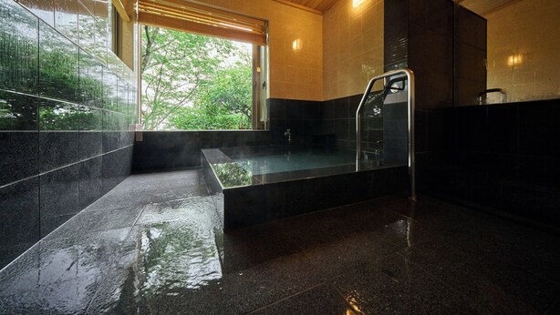 Casa de banho moderna com hidromassagem em vidro, teto de madeira e vista para árvores através de uma grande janela.