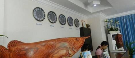 Quarto com uma grande escultura de peixe de madeira, um relógio de parede com a inscrição 'London' e uma pessoa trabalhando em uma mesa.