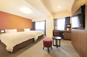 Quarto de hotel com cama de casal, uma mesinha, um banquinho vermelho, televisão e cozinha compacta.