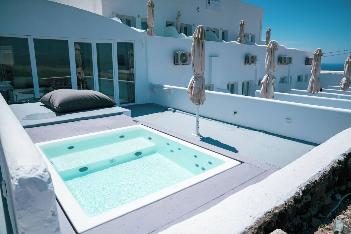 Uma área de piscina no terraço com hidromassagem, mobiliário para áreas externas e guarda-sóis.