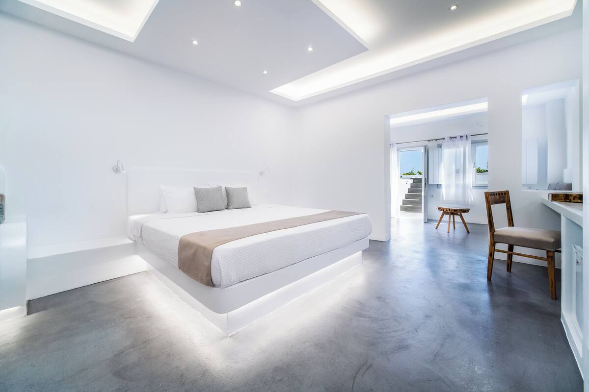 Quarto moderno com cama grande, uma cadeira de madeira e escada que dá para uma área externa.