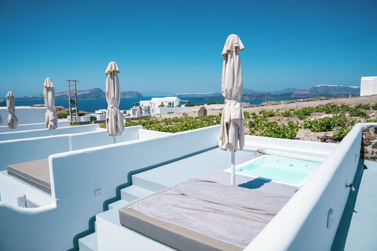 Terraço no telhado com piscina, paredes brancas e guarda-sóis.