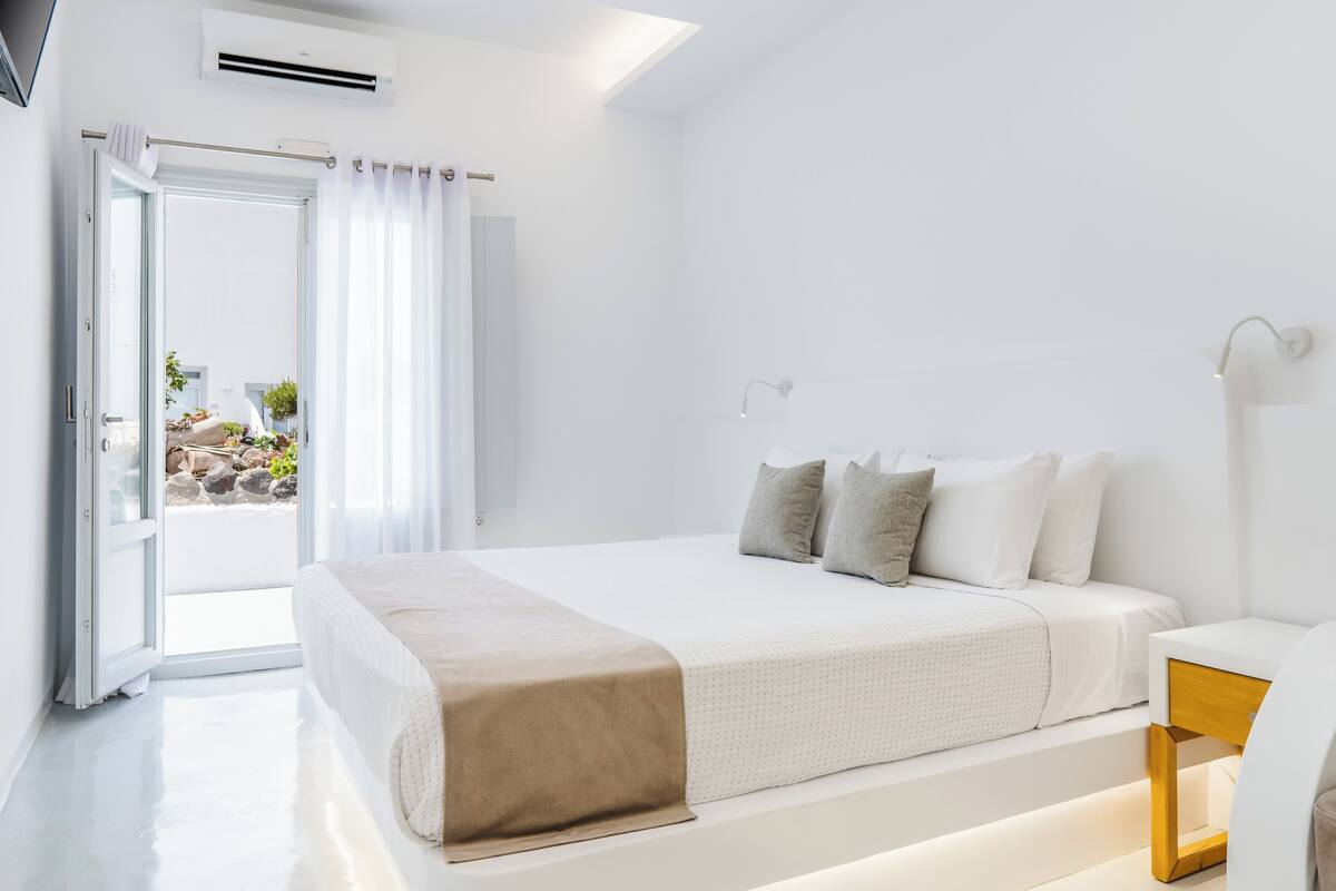 Quarto de hotel moderno com uma cama grande, uma mesa de cabeceira e vista para o exterior.