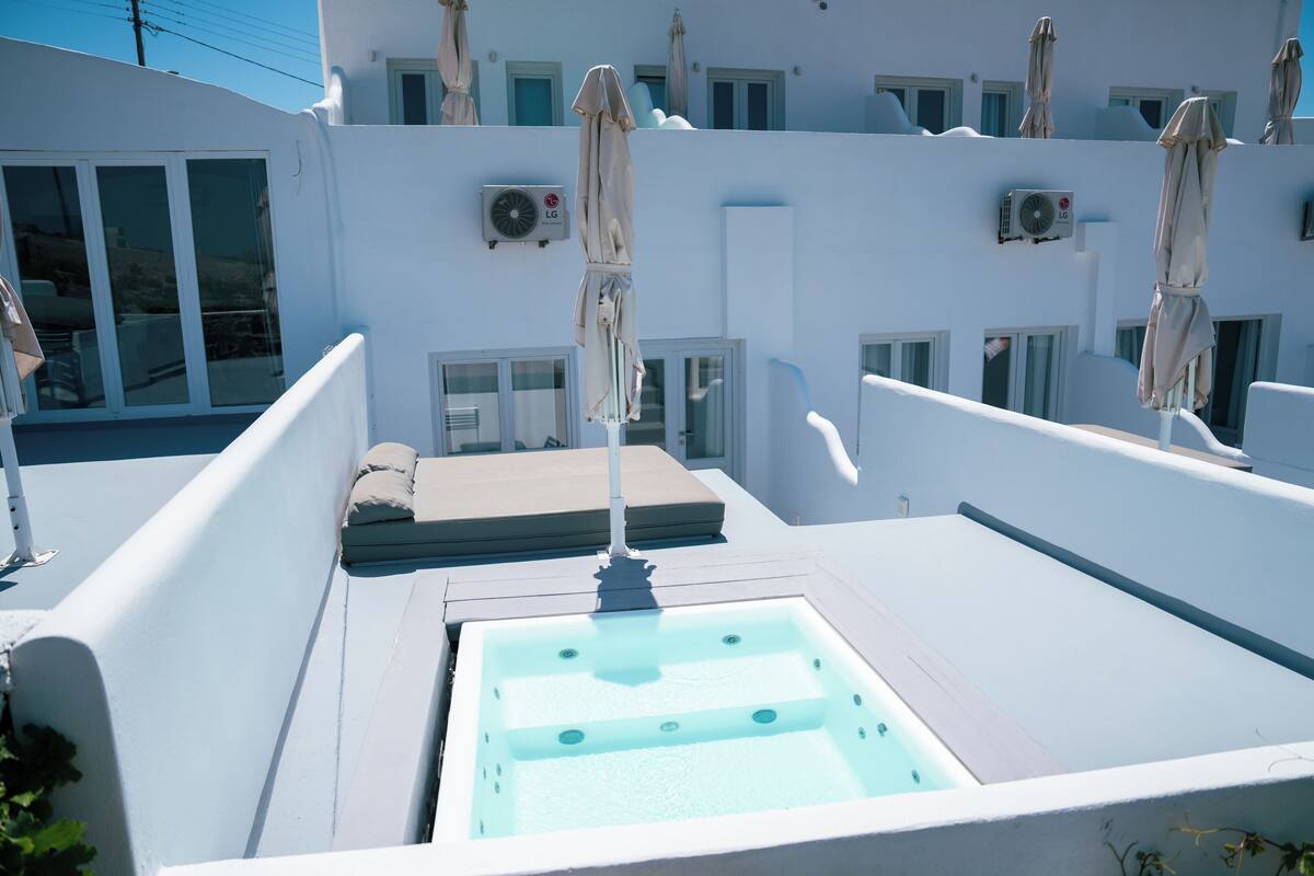 Uma área de piscina no terraço com hidromassagem, espreguiçadeiras e guarda-sóis.
