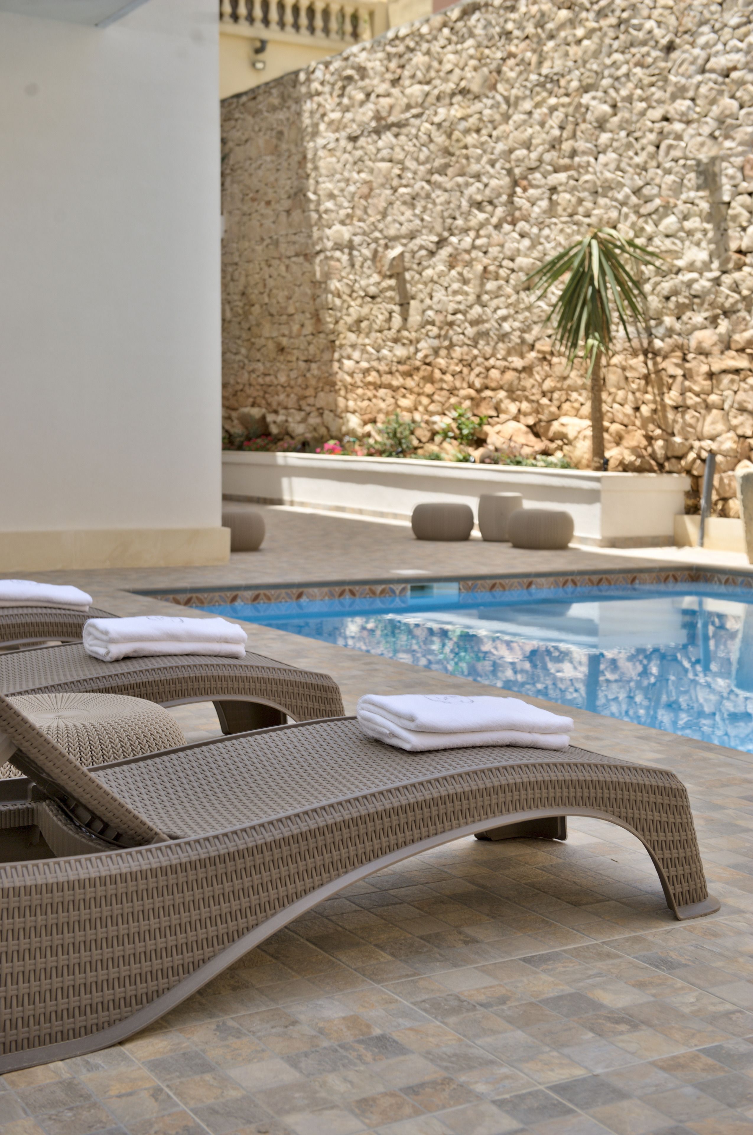 Uma área à beira da piscina com espreguiçadeiras e um muro de pedra.