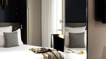 Quarto de hotel com cama, mesa de cabeceira, abajur e janela com cortinas.