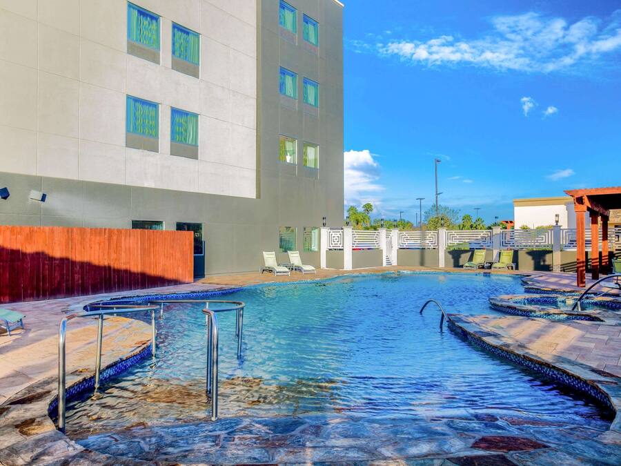 Uma área de piscina com espreguiçadeiras, um espaço de estar coberto e um edifício com várias janelas.