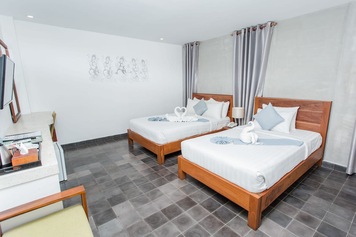 Quarto de hotel com duas camas, piso de azulejos cinza, cabeceiras de madeira, roupa de cama branca e cortinas cinza.