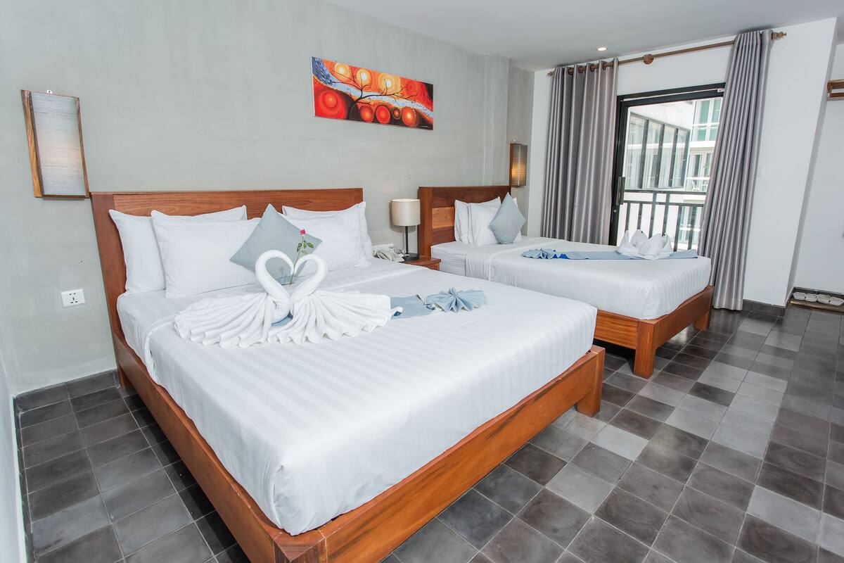 Quarto de hotel com duas camas, um quadro na parede e vista pela janela.
