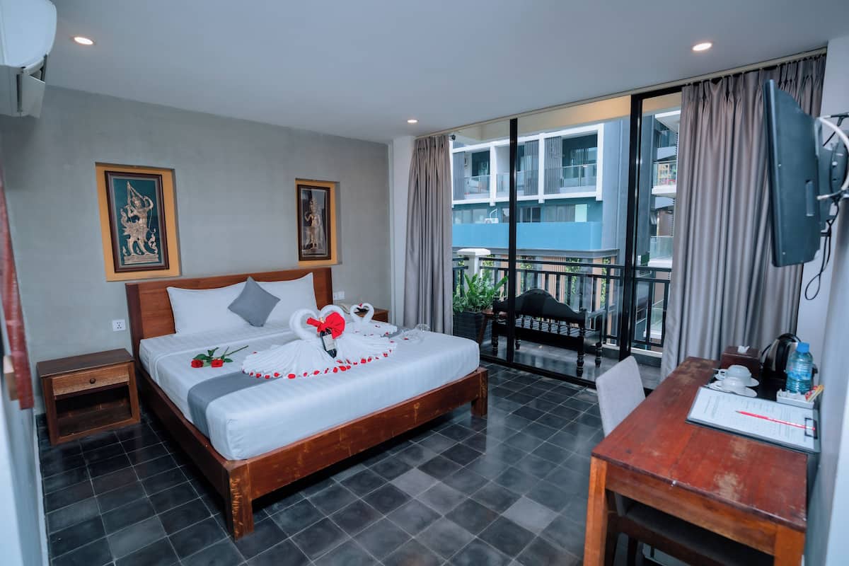 Quarto de hotel com cama, secretária, televisão e varanda com vista para edifícios.