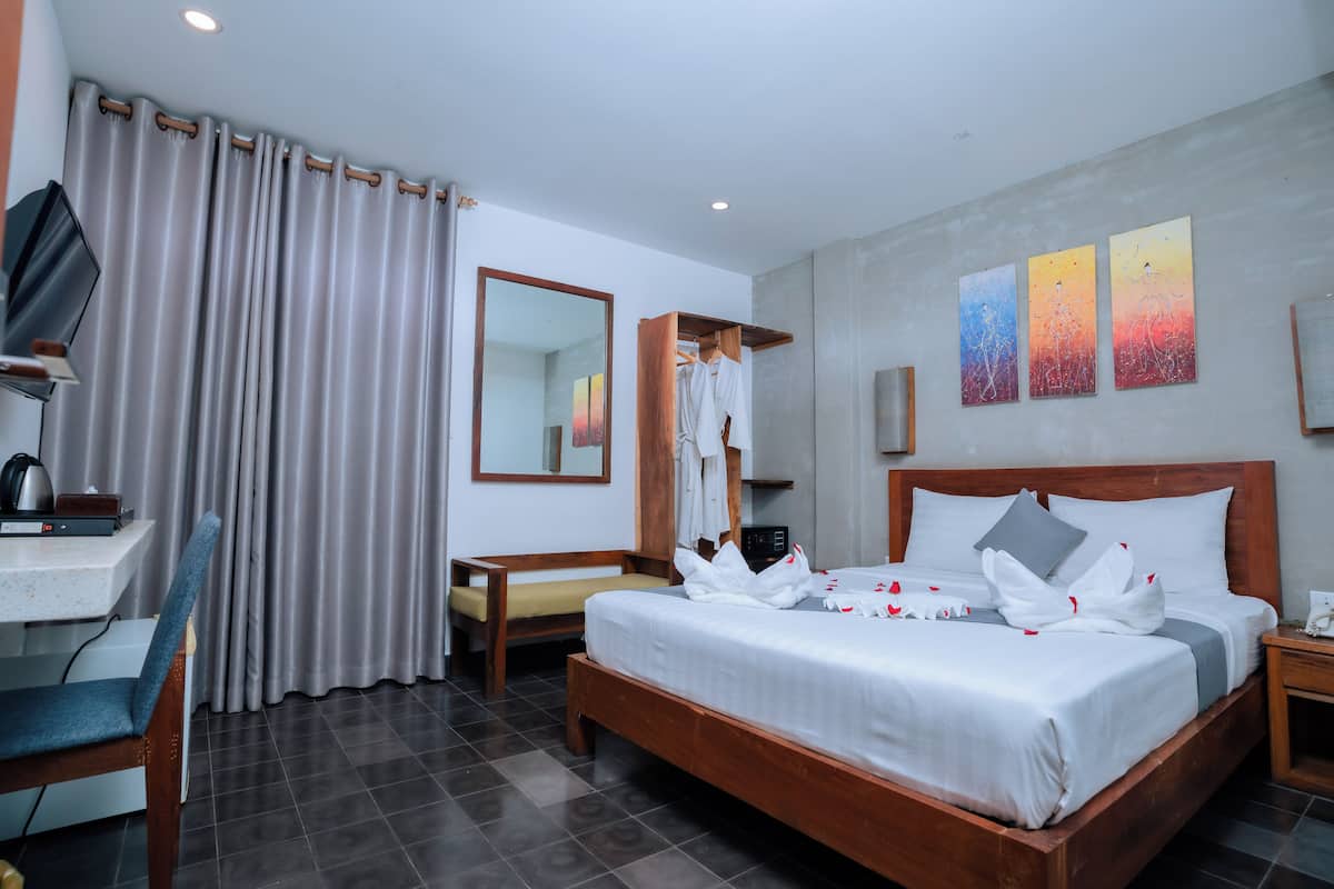 Quarto de hotel com cama de madeira, escrivaninha com cadeira, televisão e uma grande janela com cortinas.