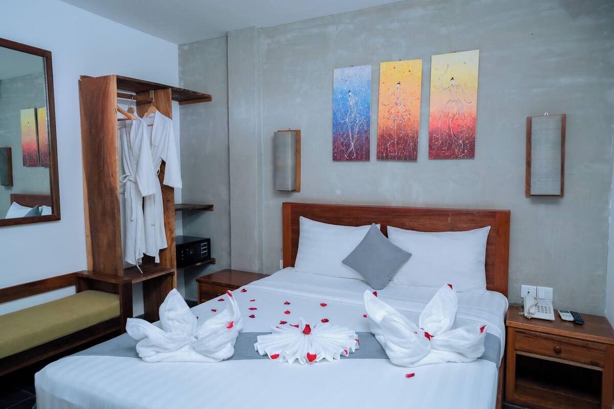 Quarto de hotel com cama bem arrumada, guarda-roupa de madeira, mesa de cabeceira com telefone e parede com três quadros.