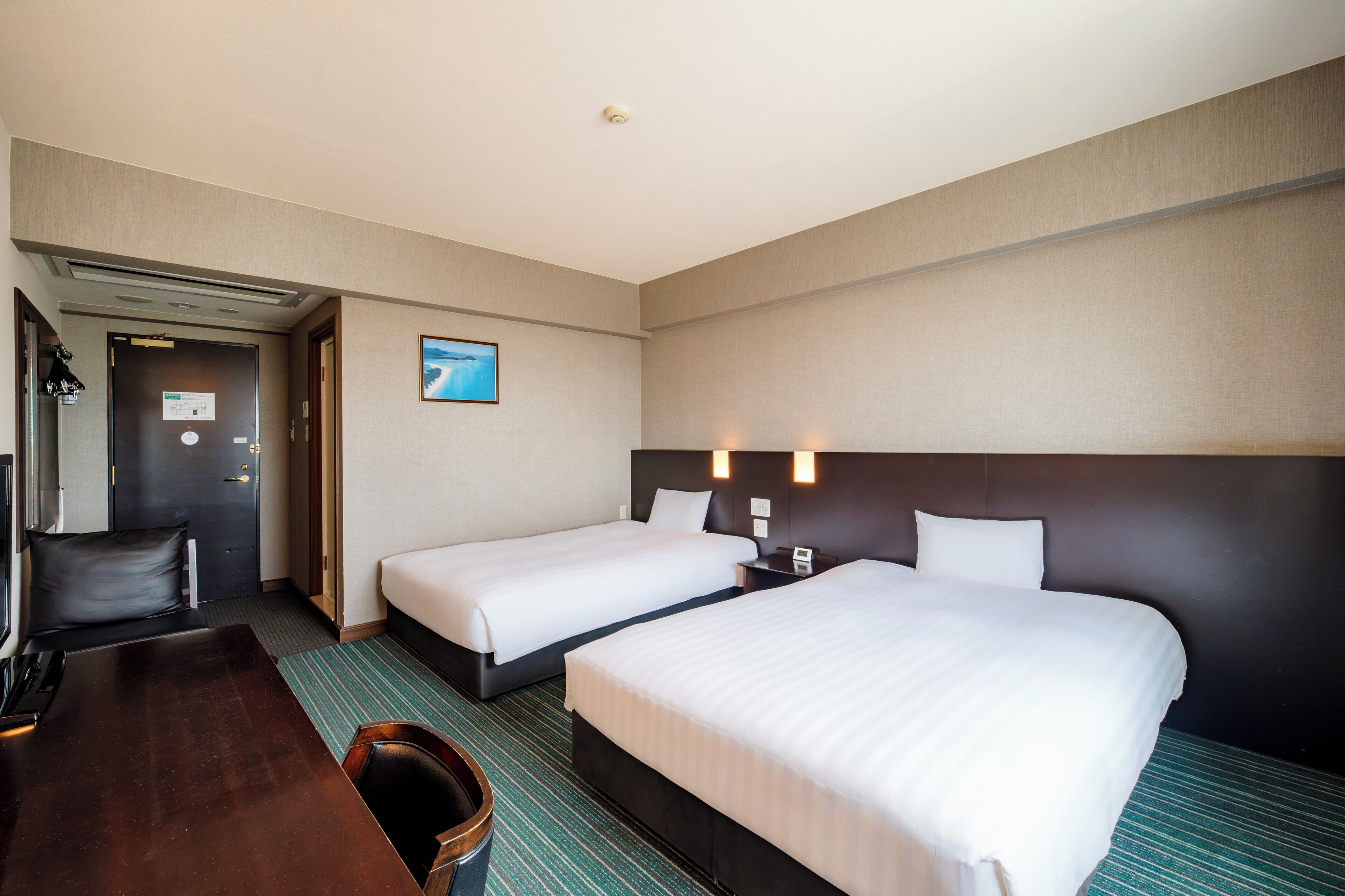 Quarto de hotel com duas camas, uma escrivaninha e uma cadeira.