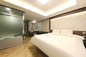 Quarto de hotel moderno com uma cama grande, banheiro com espelho e uma pequena área de estar.