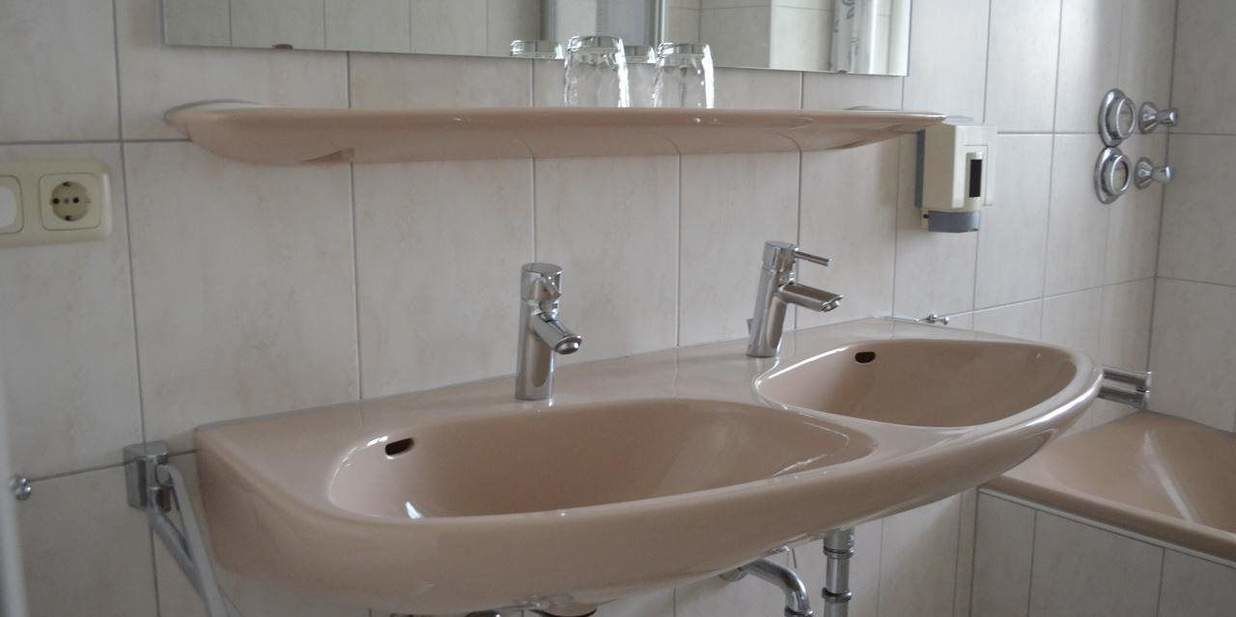 Casa de banho com duas pias, um espelho e uma prateleira acima do espelho.
