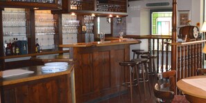 Uma área de bar com balcão de madeira, banquetes e prateleiras com copos e garrafas.