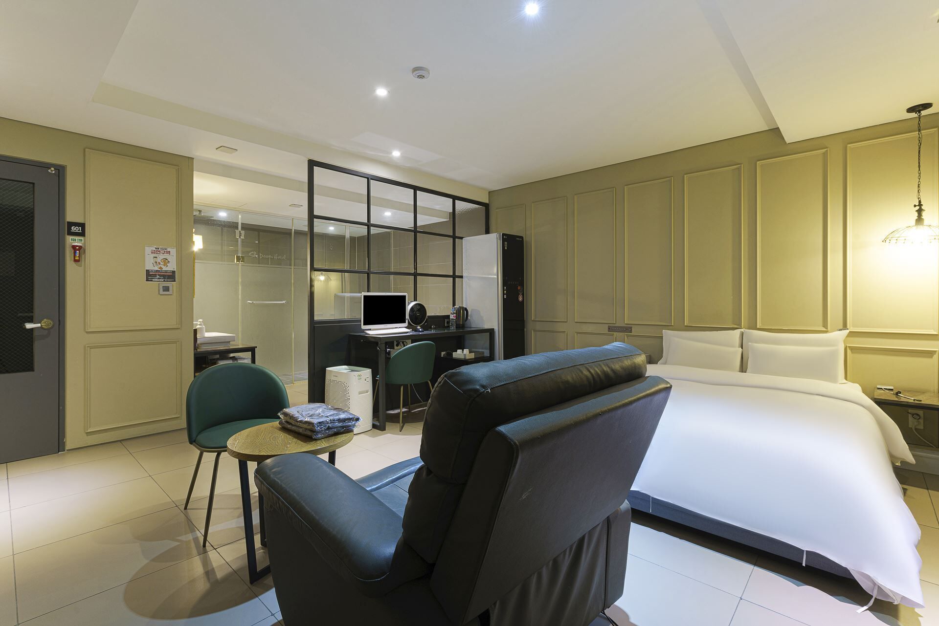 Quarto de hotel com cama, secretária com computador, cadeira e mesa pequena.