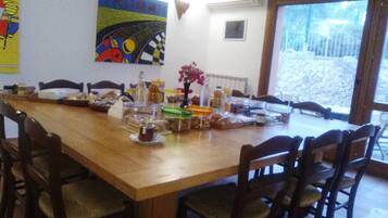 Uma sala de jantar com uma mesa de madeira comprida, cadeiras, um quadro e diversos alimentos.