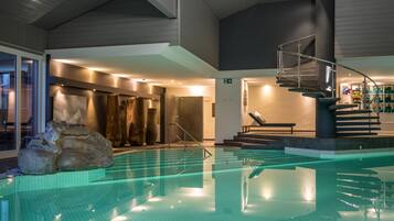 Uma piscina interior moderna com piso de vidro, escada em espiral e parede de pedra.
