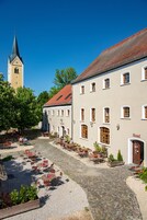 Um hotel com telhado de telhas vermelhas, uma igreja com uma torre e área externa com mesas e cadeiras.