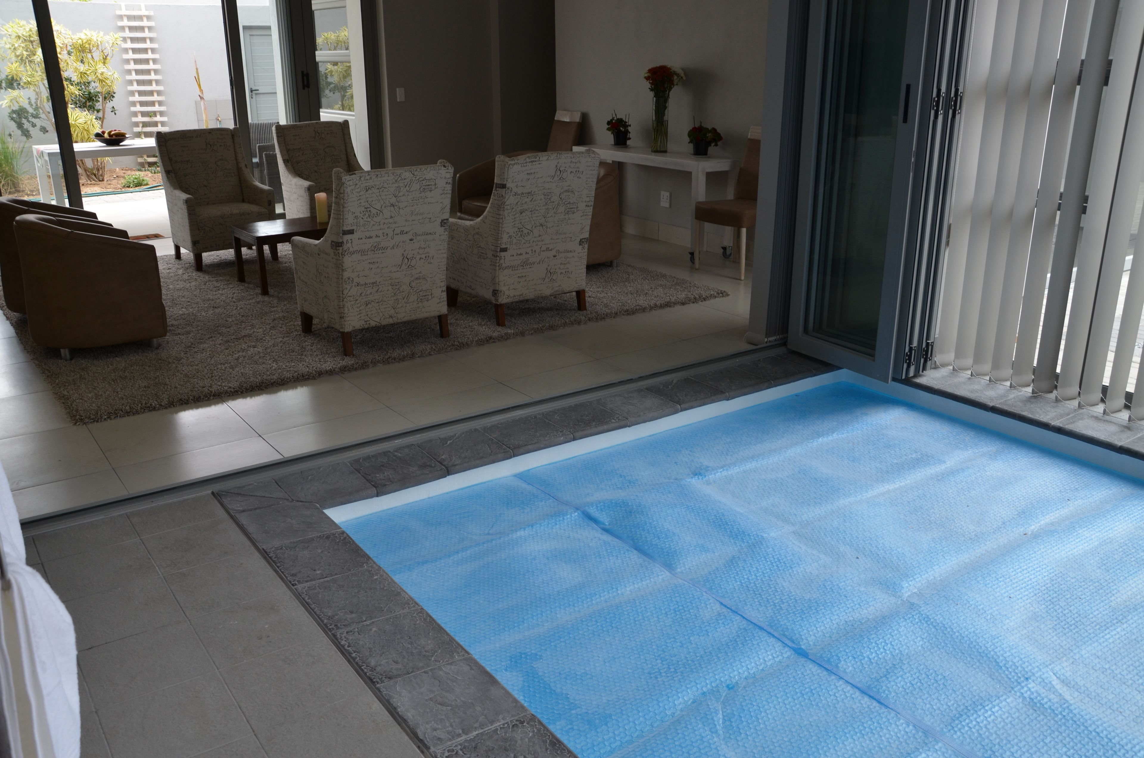 Uma sala de estar moderna com área de piscina, incluindo um espaço de estar e vista pela porta de vidro.