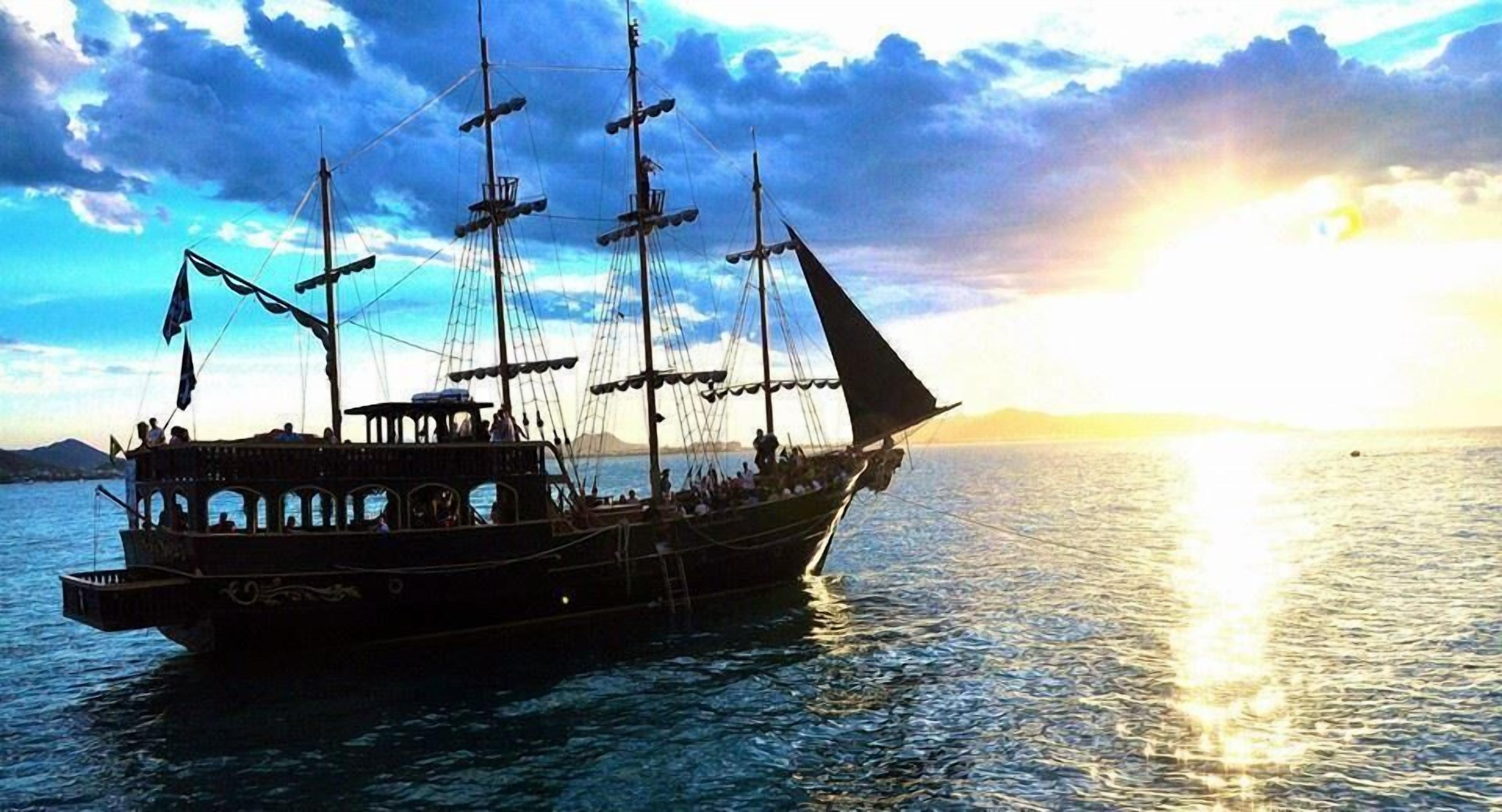 Um grande navio a vela com vários mastros e estrutura de cabine, navegando em águas calmas.